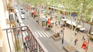 Uma rua urbana movimentada com lojas, pedestres e veículos estacionados.