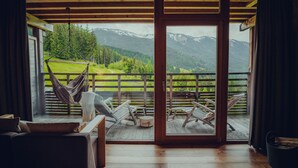 Um deck de madeira com uma rede e espreguiçadeiras, com vista para uma paisagem montanhosa.