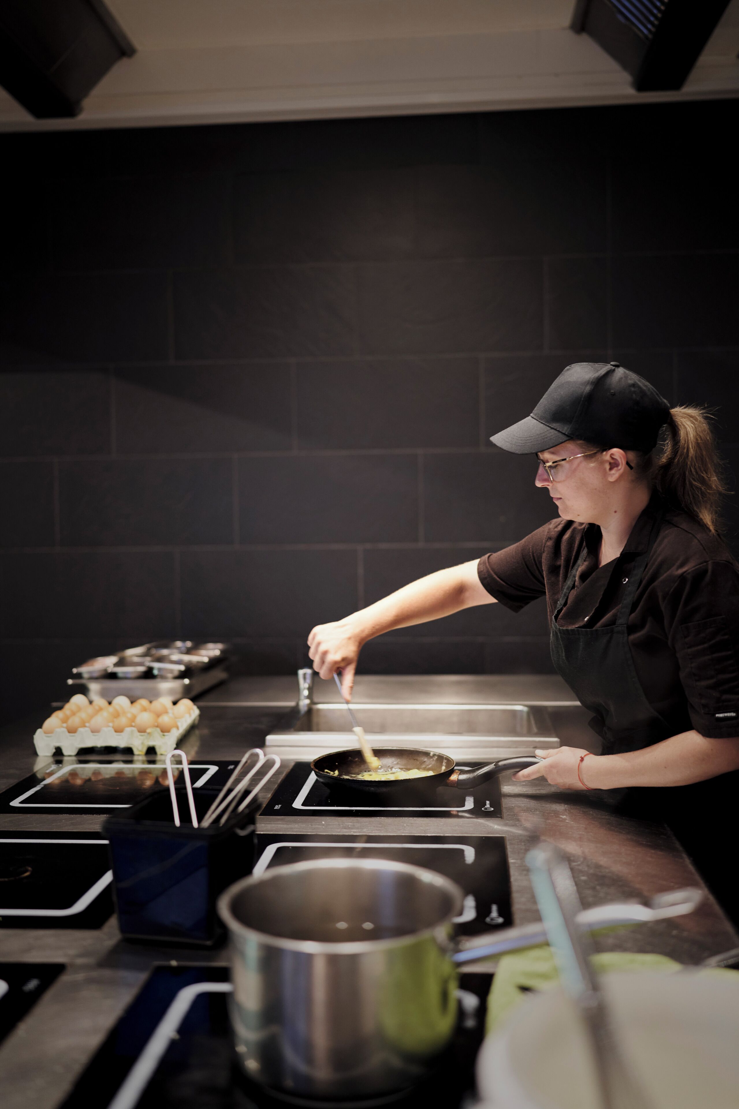 Uma pessoa cozinhando em uma cozinha, com fogão, panelas e bandejas de ovos.