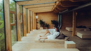 Interior em madeira com uma parede de vidro, soalho de madeira e uma pessoa deitada numa cama.
