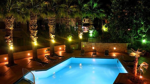 Piscina externa com espreguiçadeiras e palmeiras, cercada por paredes de pedra e iluminação suave.