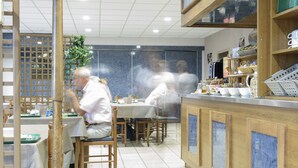 Um restaurante com mobiliário de madeira, um balcão com diversos itens e piso de azulejos.