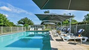 Piscina com cadeiras de sol e guarda-sóis, cercada por uma cerca e vegetação.