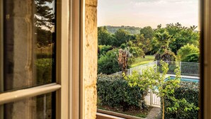 Vista da janela com um jardim exuberante, diversas árvores e um cercado branco.