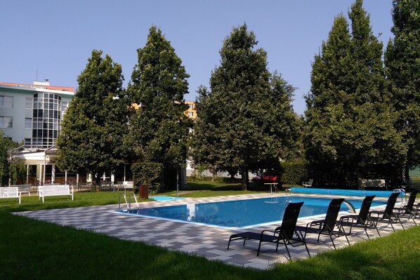 Piscina com espreguiçadeiras, rodeada por árvores e um edifício com telhado verde.
