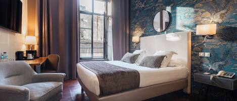 Quarto de hotel com cama, cadeira, escrivaninha, abajur e telefone.