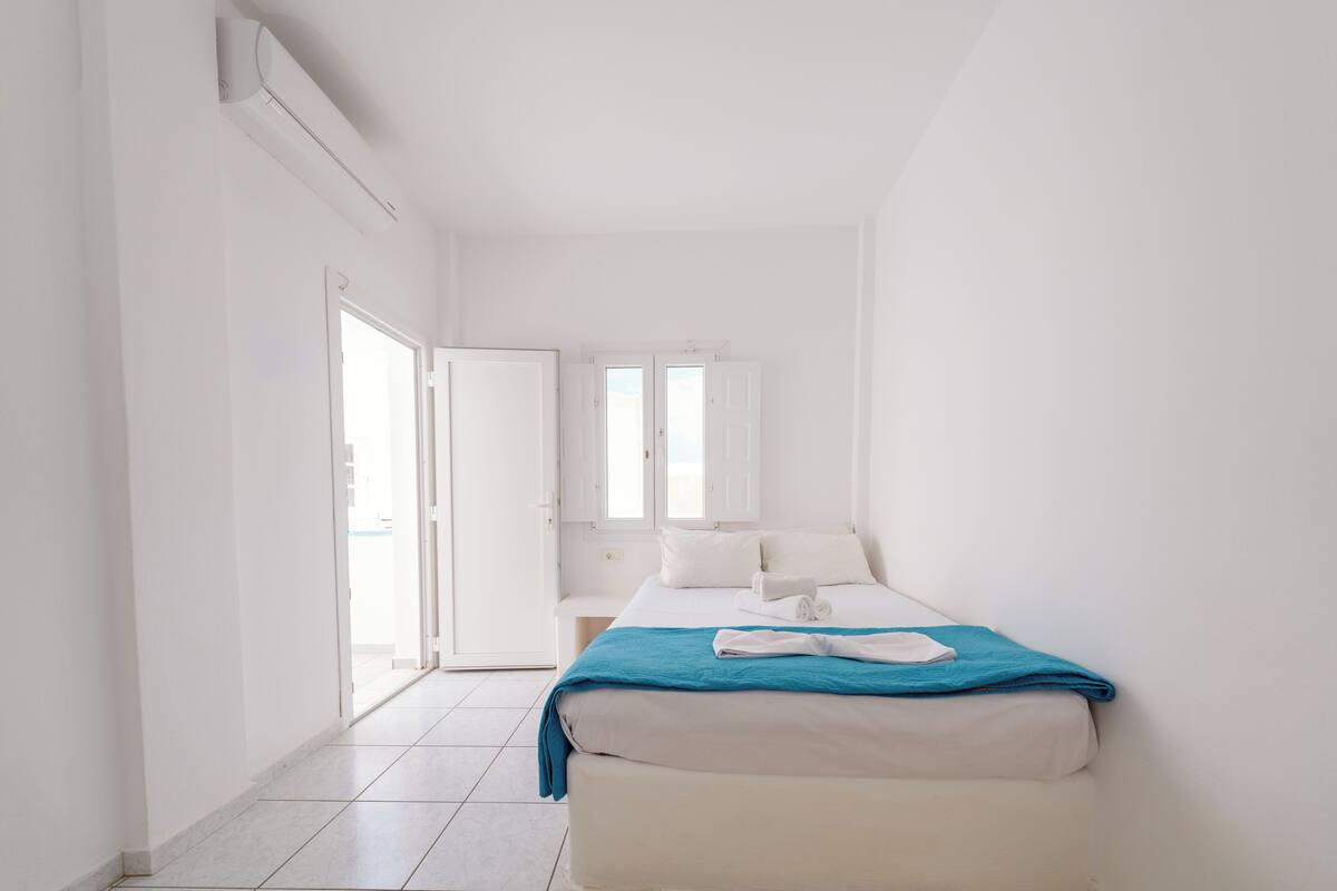 Quarto de hotel com cama, escrivaninha e uma cadeira.