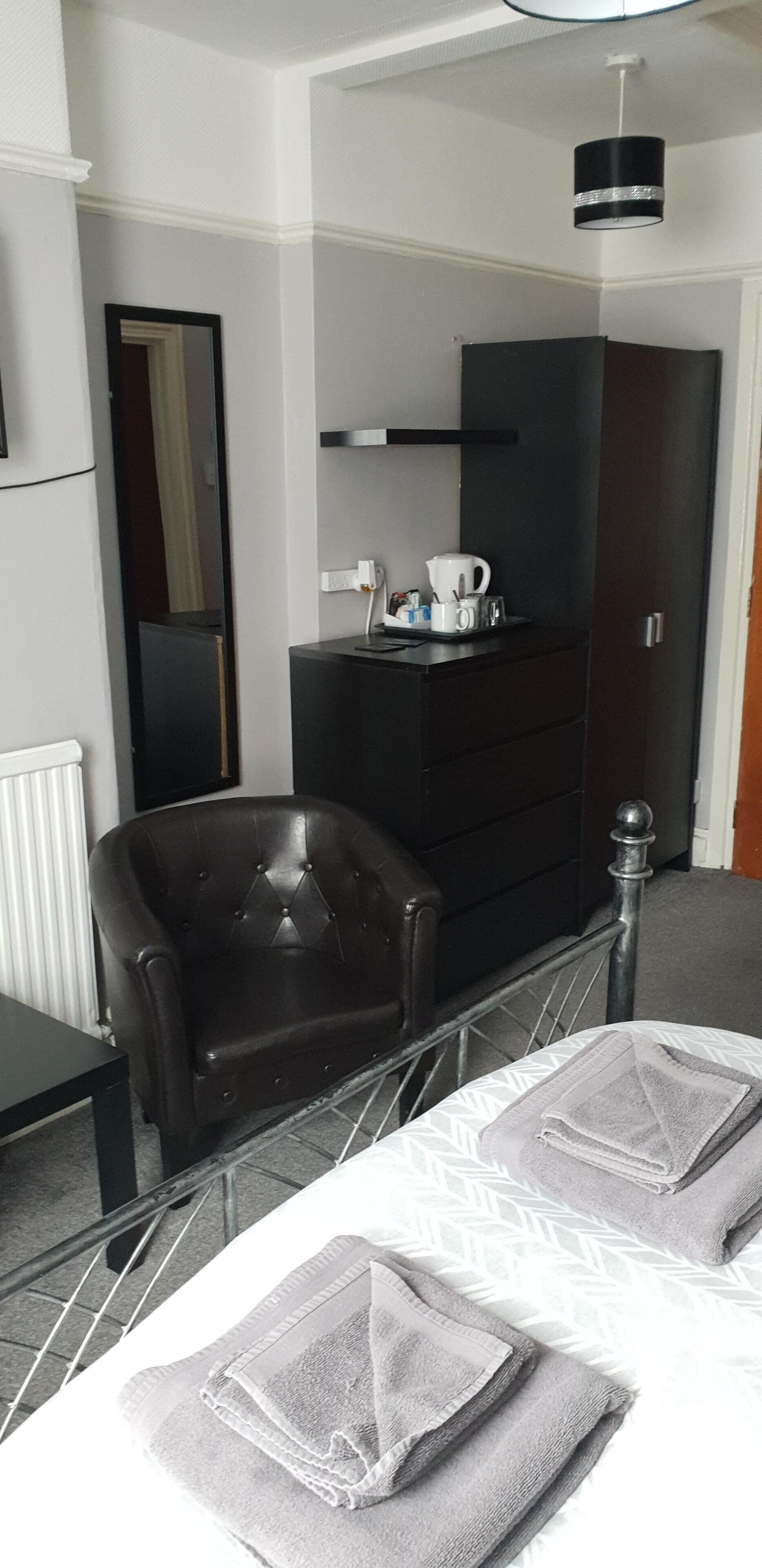 Quarto de hotel com cama, cadeira, guarda-roupa, espelho e luminária pendente.