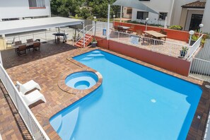 Piscina com área central rebaixada, rodeada por um deck de tijolos e grades brancas.