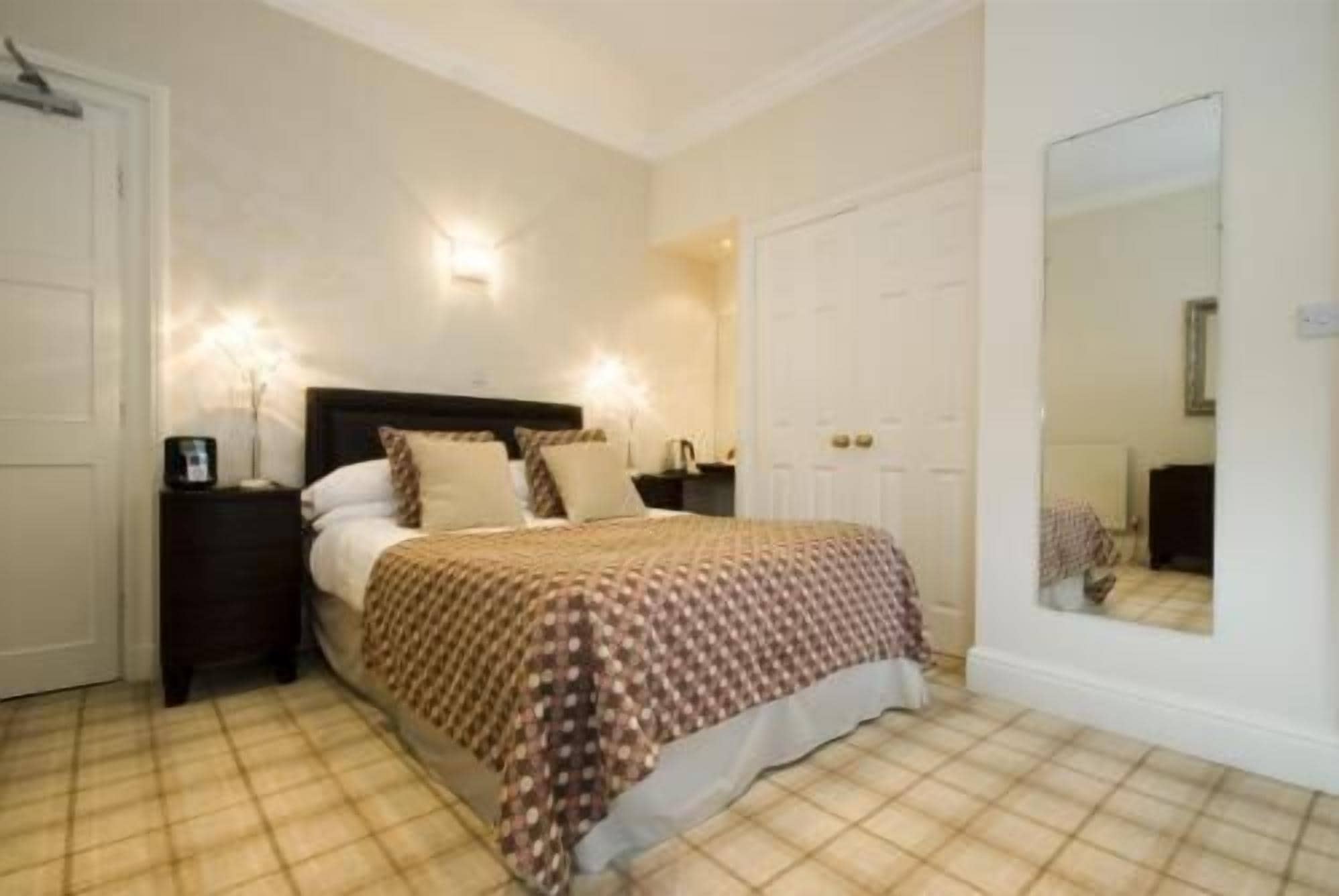 Quarto com cama, mesas de cabeceira, espelho e porta.