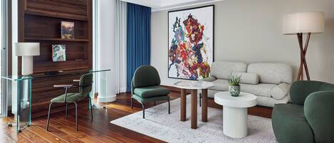 Uma sala de estar moderna com piso de madeira, um sofá verde, uma mesa de centro branca, uma poltrona verde e uma mesa de vidro com uma luminária.