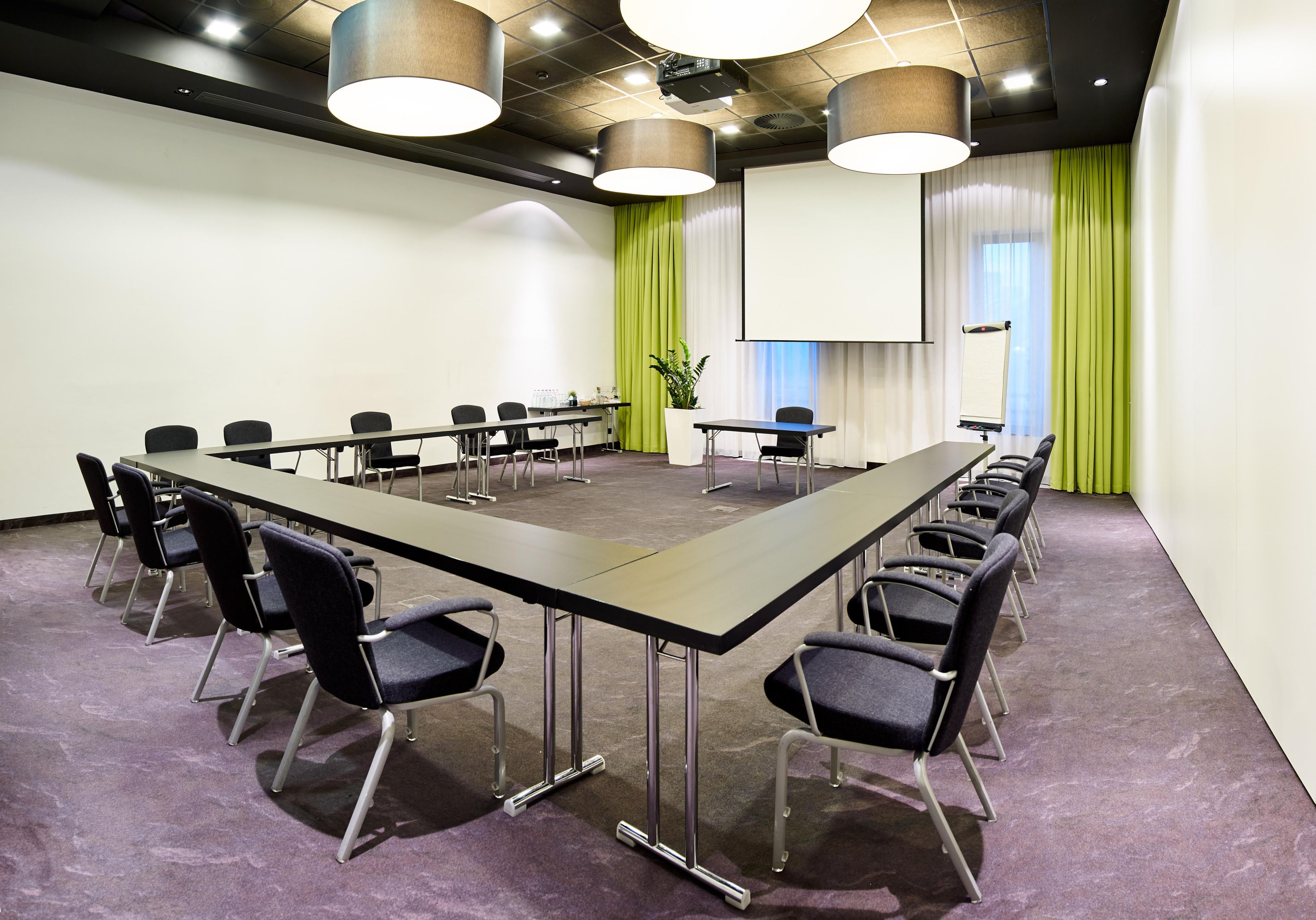 Sala de conferências com uma mesa comprida, cadeiras, um projetor e uma tela.