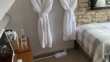 Quarto de hotel com cama, penteadeira de madeira, escrivaninha com um laptop e controles remotos, e dois roupões brancos pendurados em um suporte.