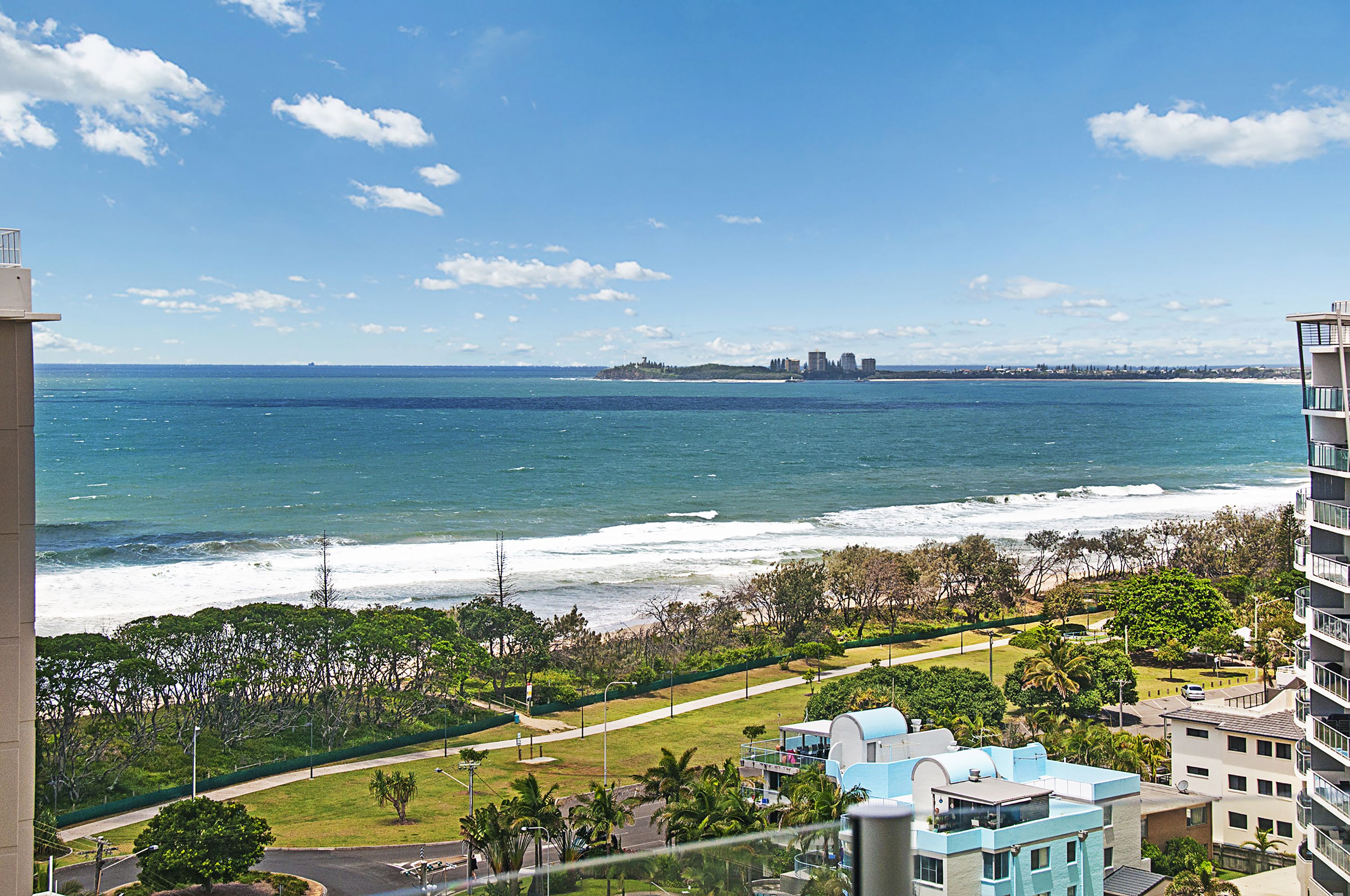 Vista costeira com praia, linha do horizonte urbana à distância e mistura de edifícios residenciais e comerciais.