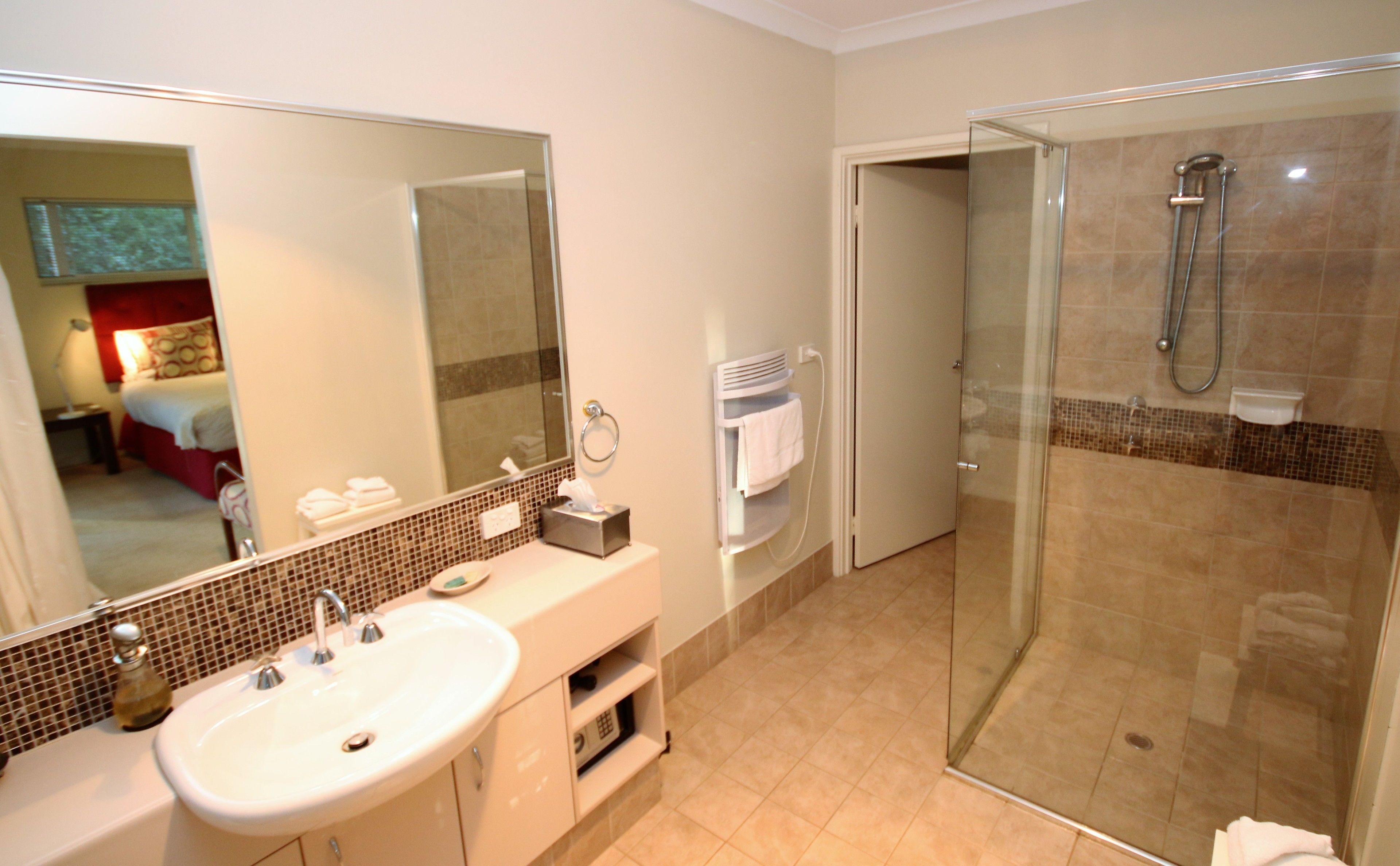 Um banheiro moderno com um espelho grande, duas pias, um chuveiro com divisória de vidro e piso revestido de azulejos.