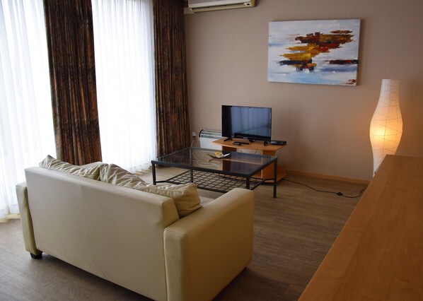 Sala de estar com sofá, mesa de centro de vidro, televisão e abajur.