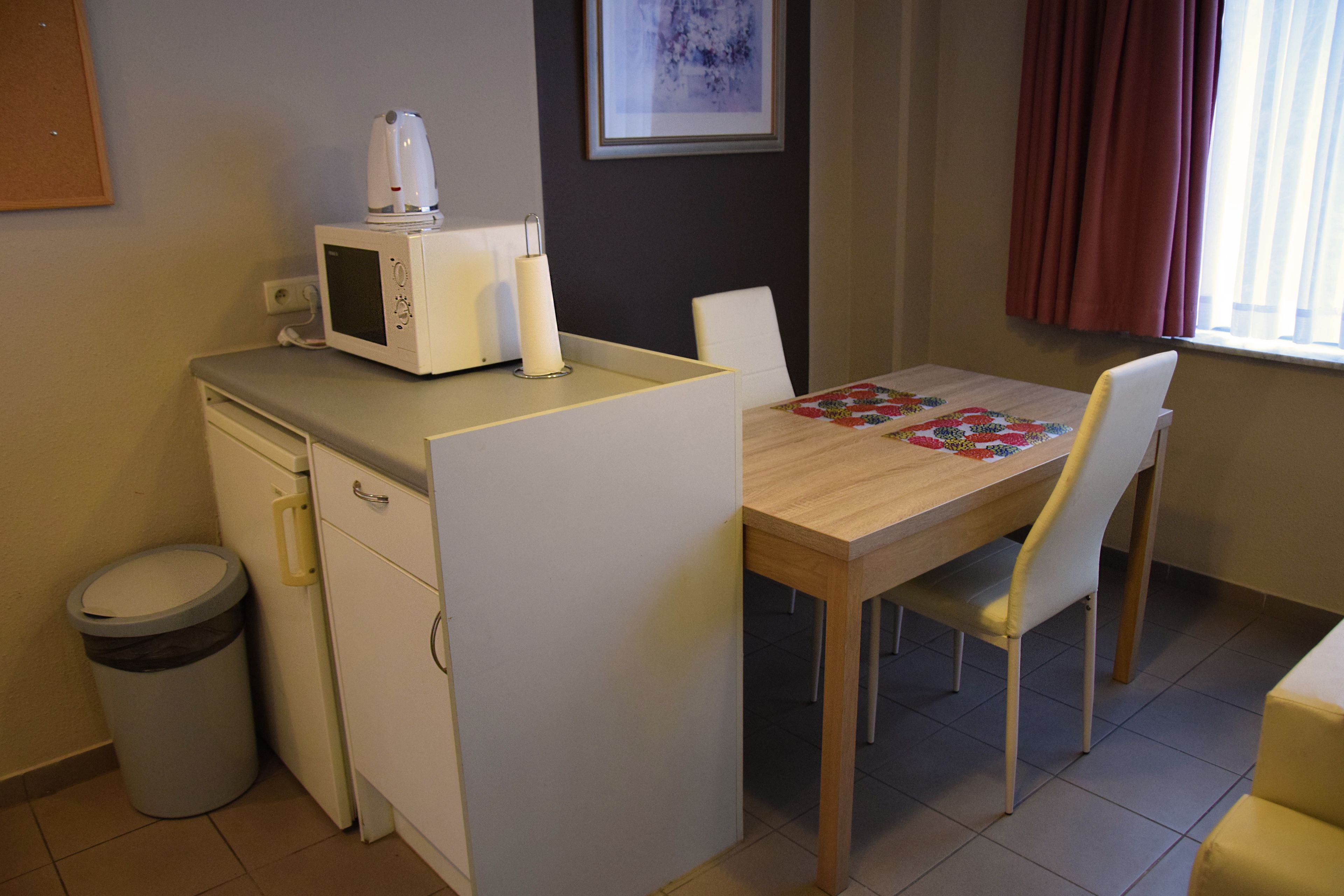 Uma cozinha compacta com micro-ondas, uma pequena lixeira e uma mesa com cadeiras.