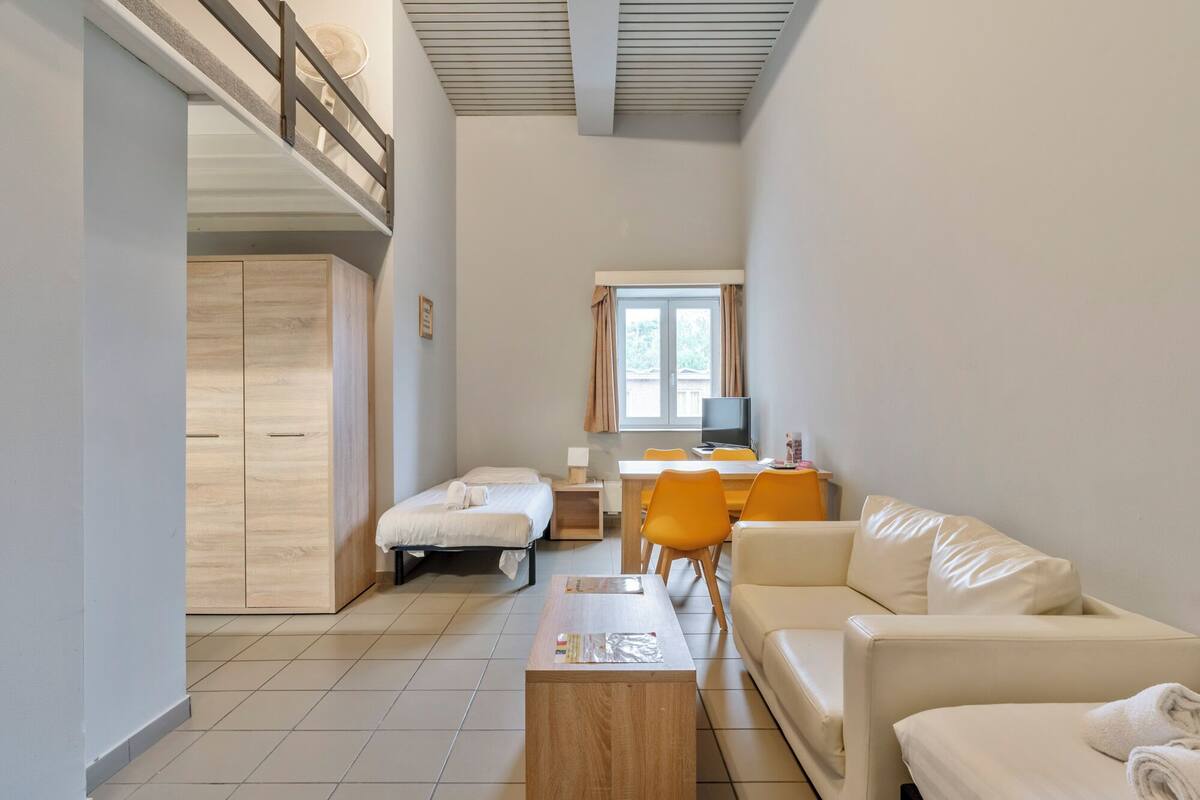 Quarto moderno com cama, sofá, mesa de jantar com cadeiras, televisão e janela com cortinas.