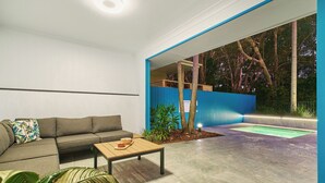 Uma sala de estar moderna com um sofá seccional, uma mesa de centro e vista para uma piscina e árvores.