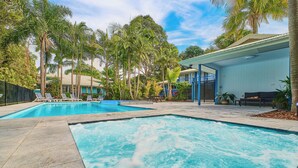 Uma área de piscina com duas piscinas, espreguiçadeiras e palmeiras.