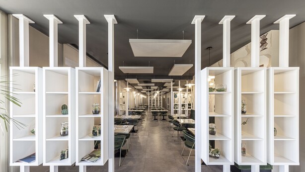 Uma biblioteca ampla com estantes brancas e mesas, com livros e objetos decorativos.