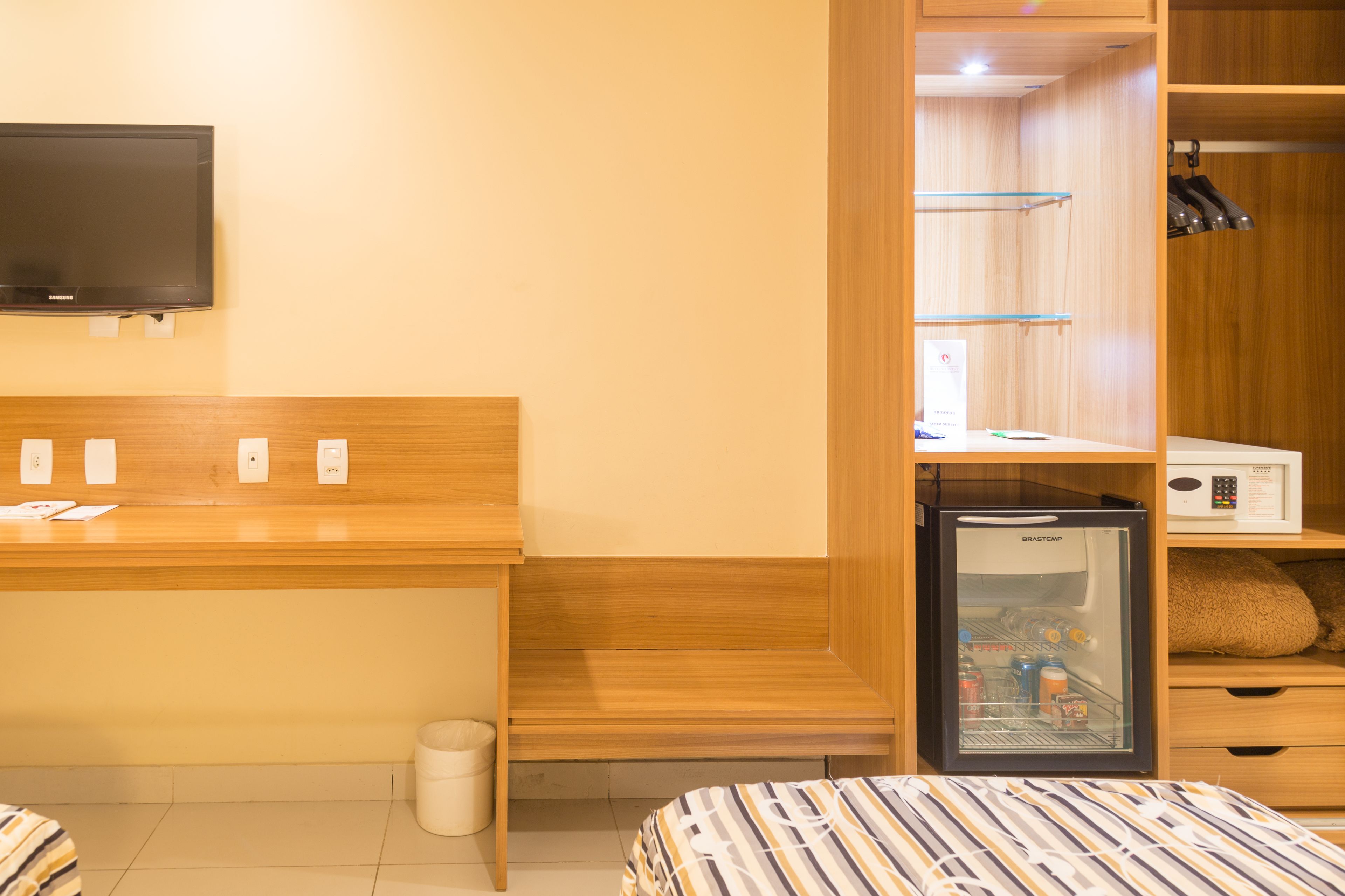 Quarto de hotel com secretária de madeira, televisão, minibar e cama com roupa de cama listrada.
