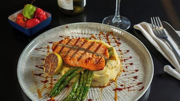 Prato com salmão grelhado, aspargos e uma fatia de limão, acompanhado de uma garrafa de vinho e um copo.