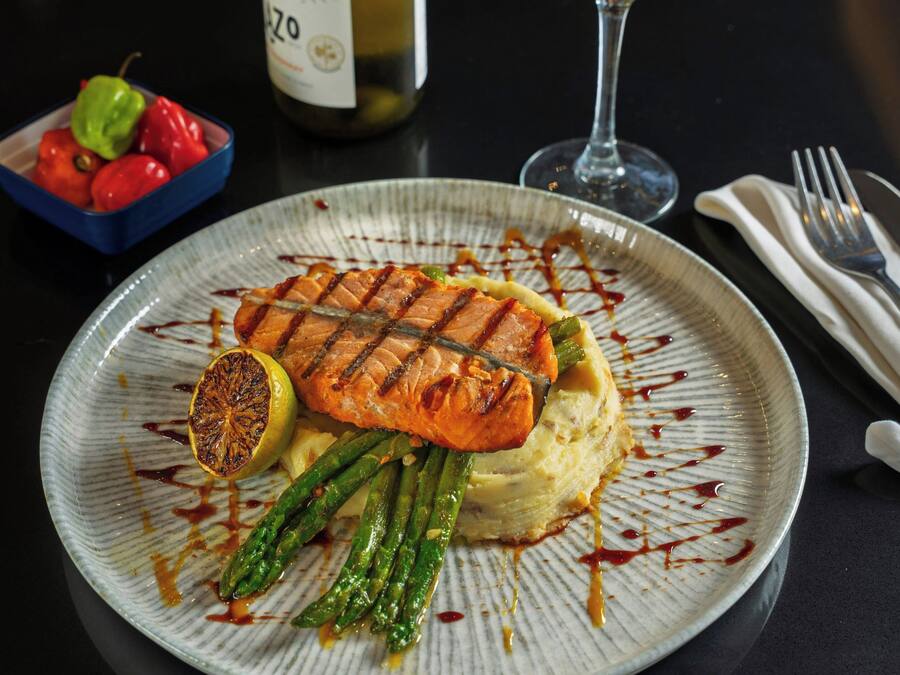 Prato com salmão grelhado, aspargos e uma fatia de limão, acompanhado de uma garrafa de vinho e um copo.