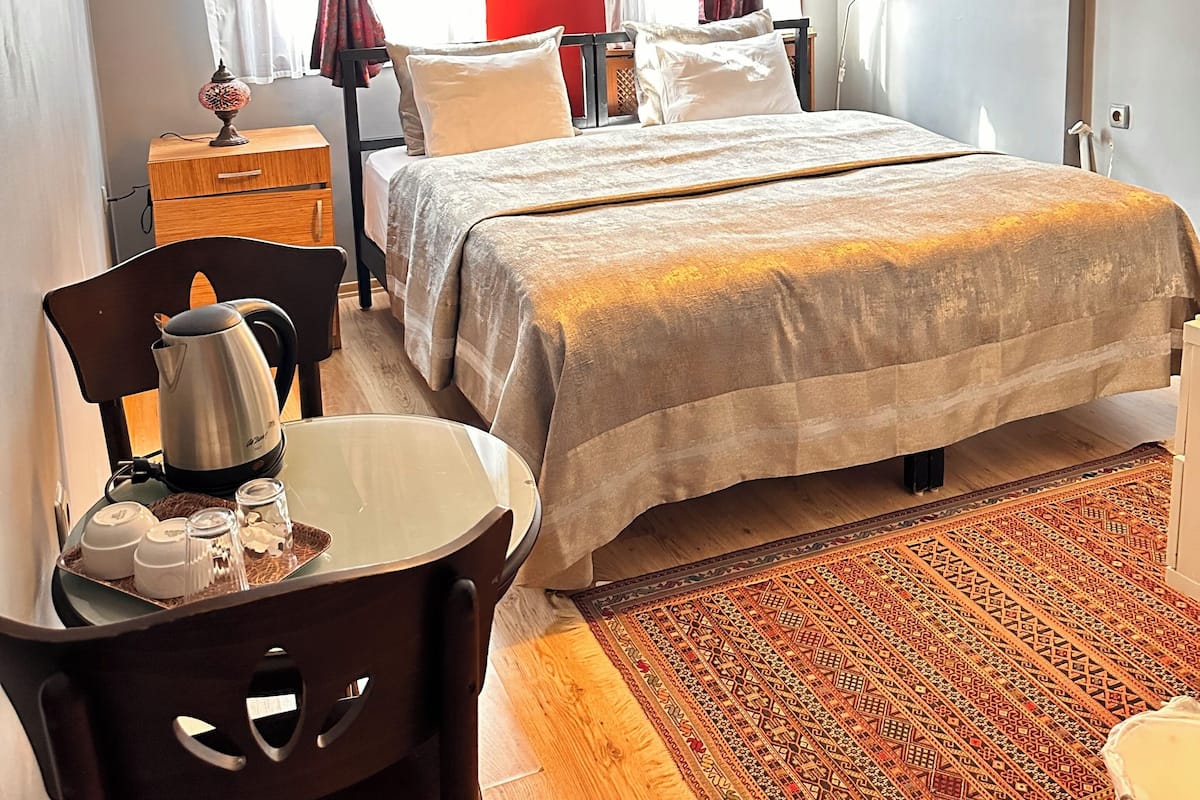 Quarto com cama, cadeira, mesa com chaleira, luminária e tapete.