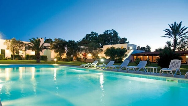 Piscina com espreguiçadeiras e um edifício ao fundo.