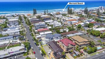 Vista aérea de uma área residencial costeira com casas, lojas e a Praia Mermaid indicada.