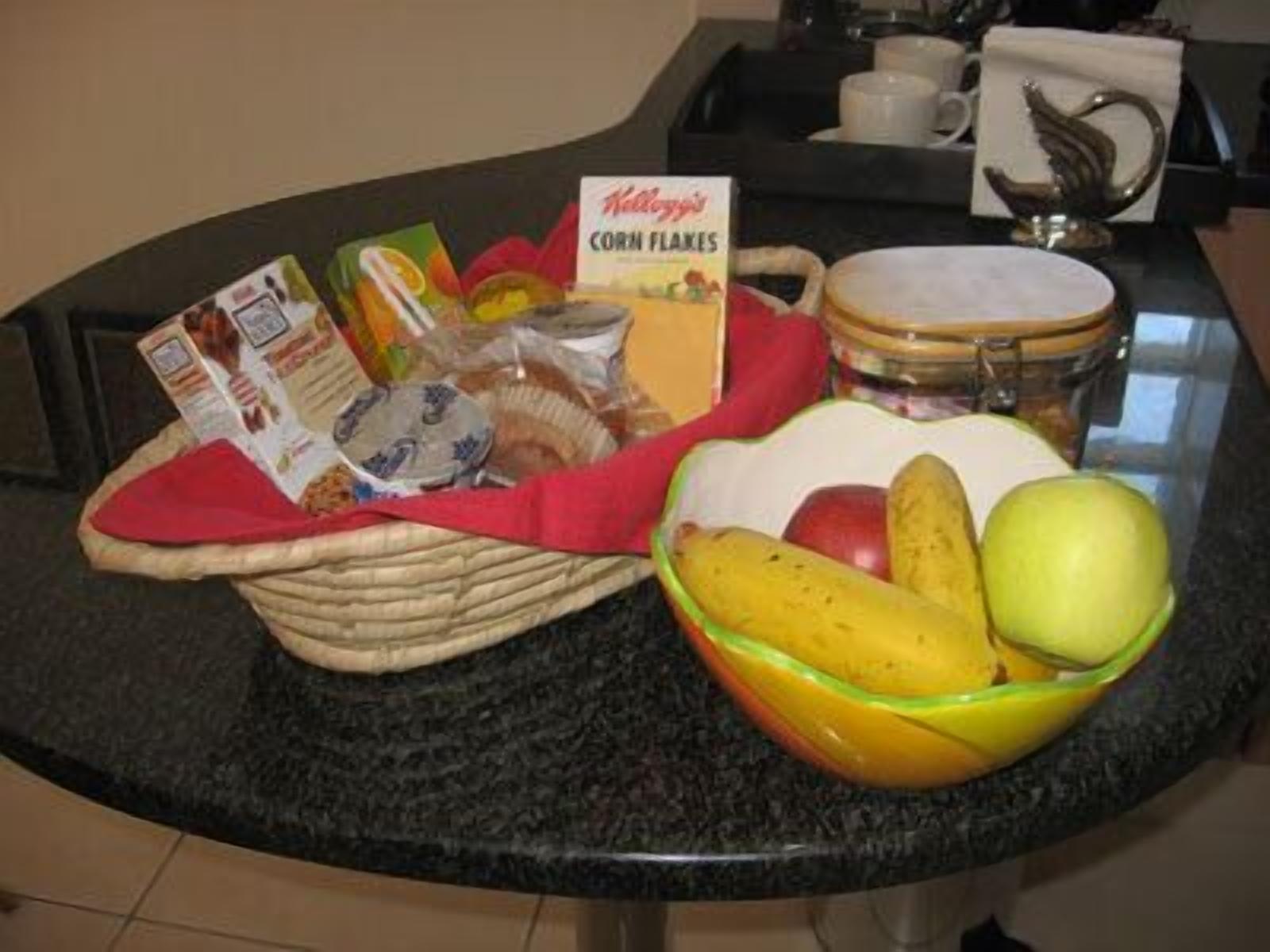 Uma bancada de cozinha com uma cesta contendo caixas de cereais, uma tigela de frutas e um pote.