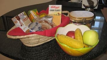 Uma bancada de cozinha com uma cesta contendo caixas de cereais, uma tigela de frutas e um pote.