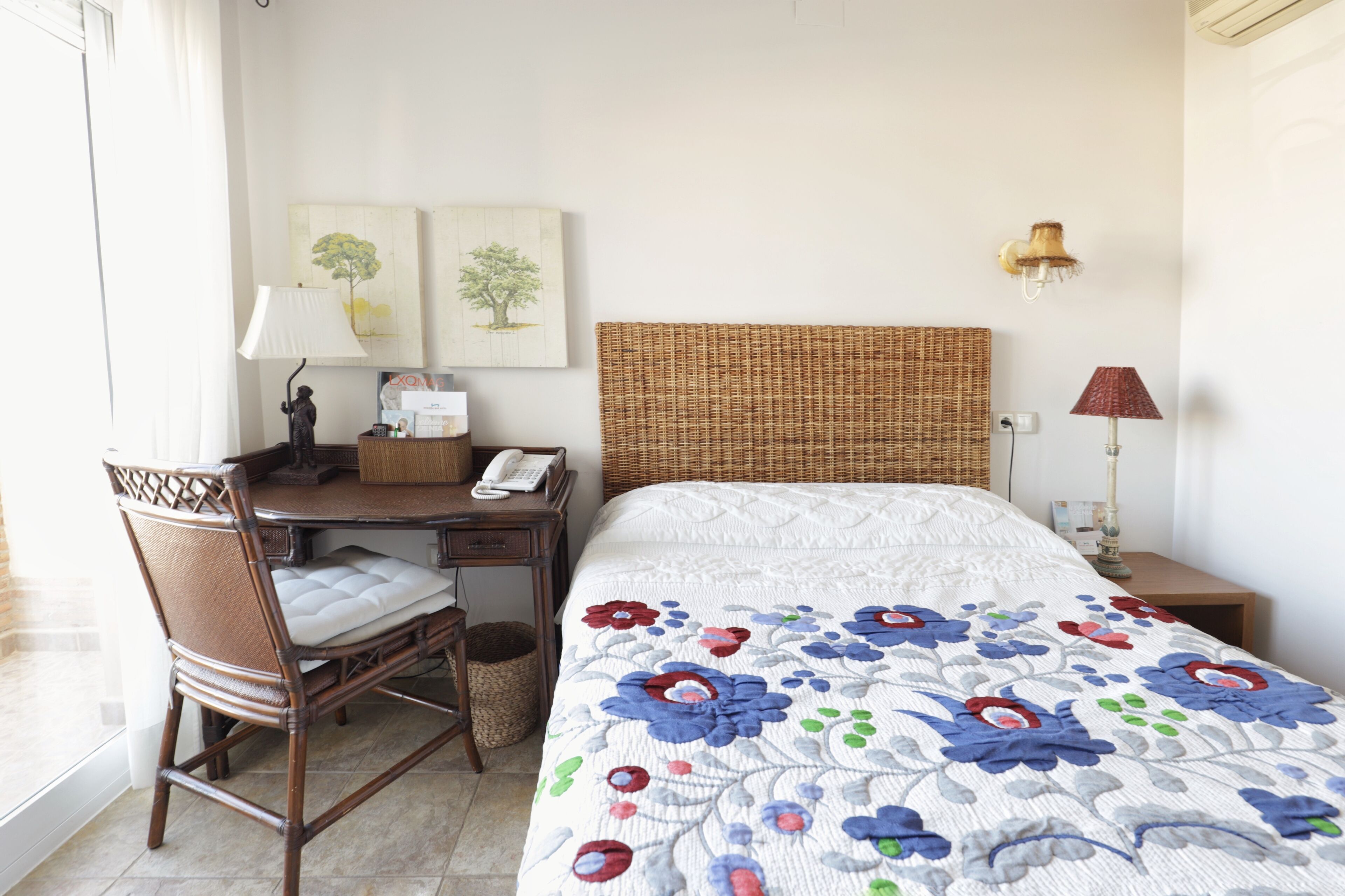 Quarto de hotel com uma cama, uma escrivaninha com telefone, uma cadeira e um abajur.