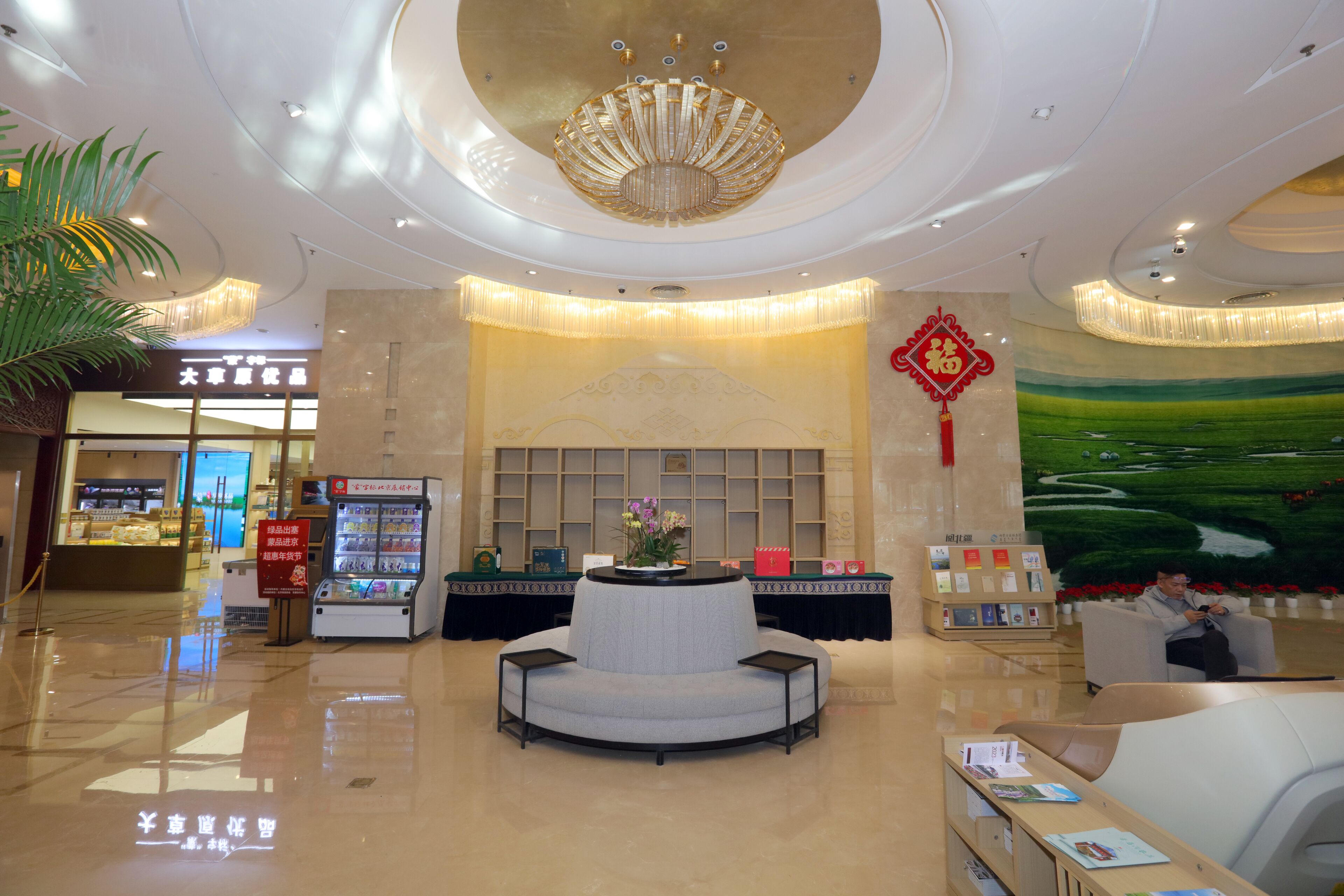 Um lobby moderno com área de estar central, um candelabro e um mural grande na parede.
