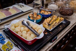 Buffet com diversos pratos, incluindo pão, doces e uma variedade de acompanhamentos.
