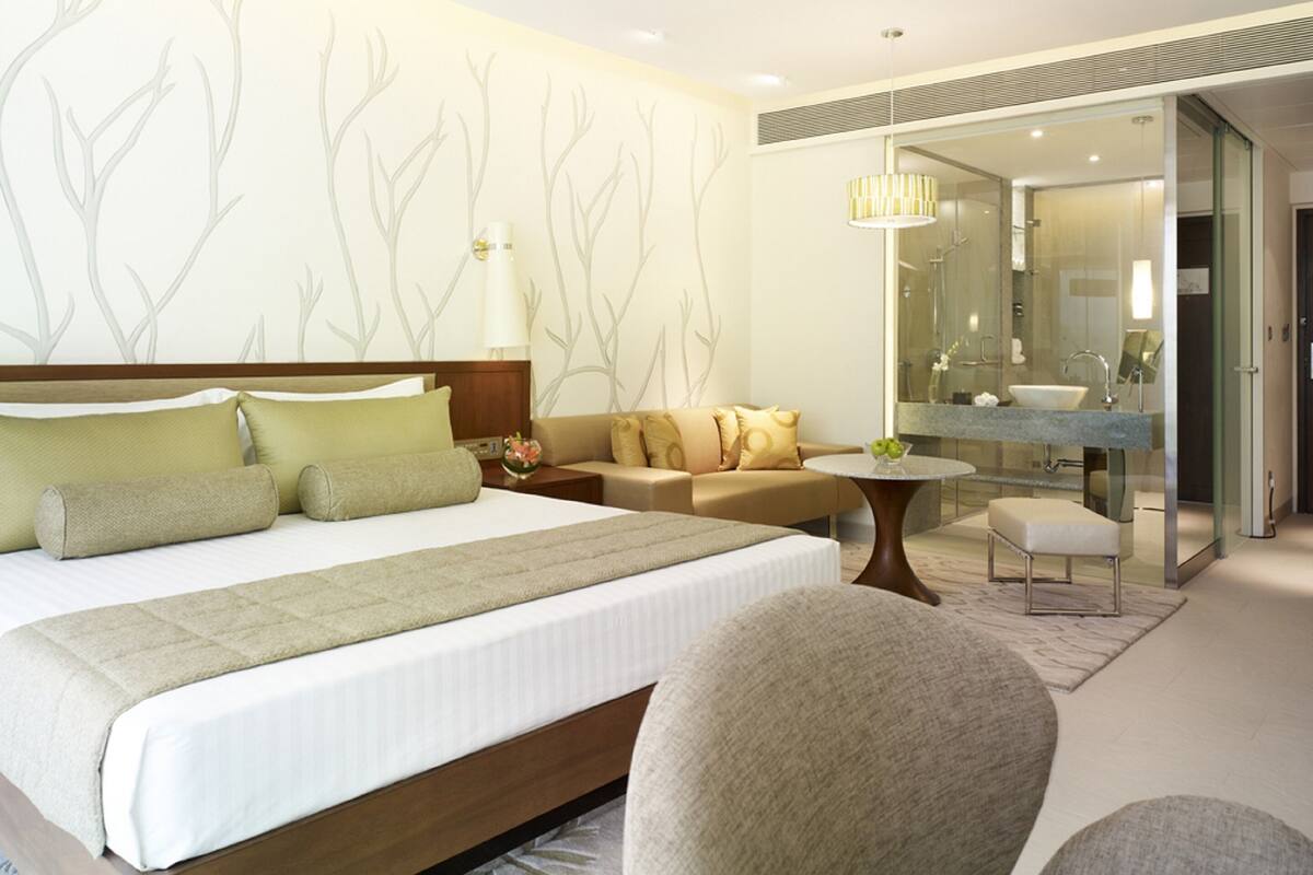 Quarto de hotel moderno com uma cama grande, um sofá, uma mesinha e um banheiro com espelho e pia.