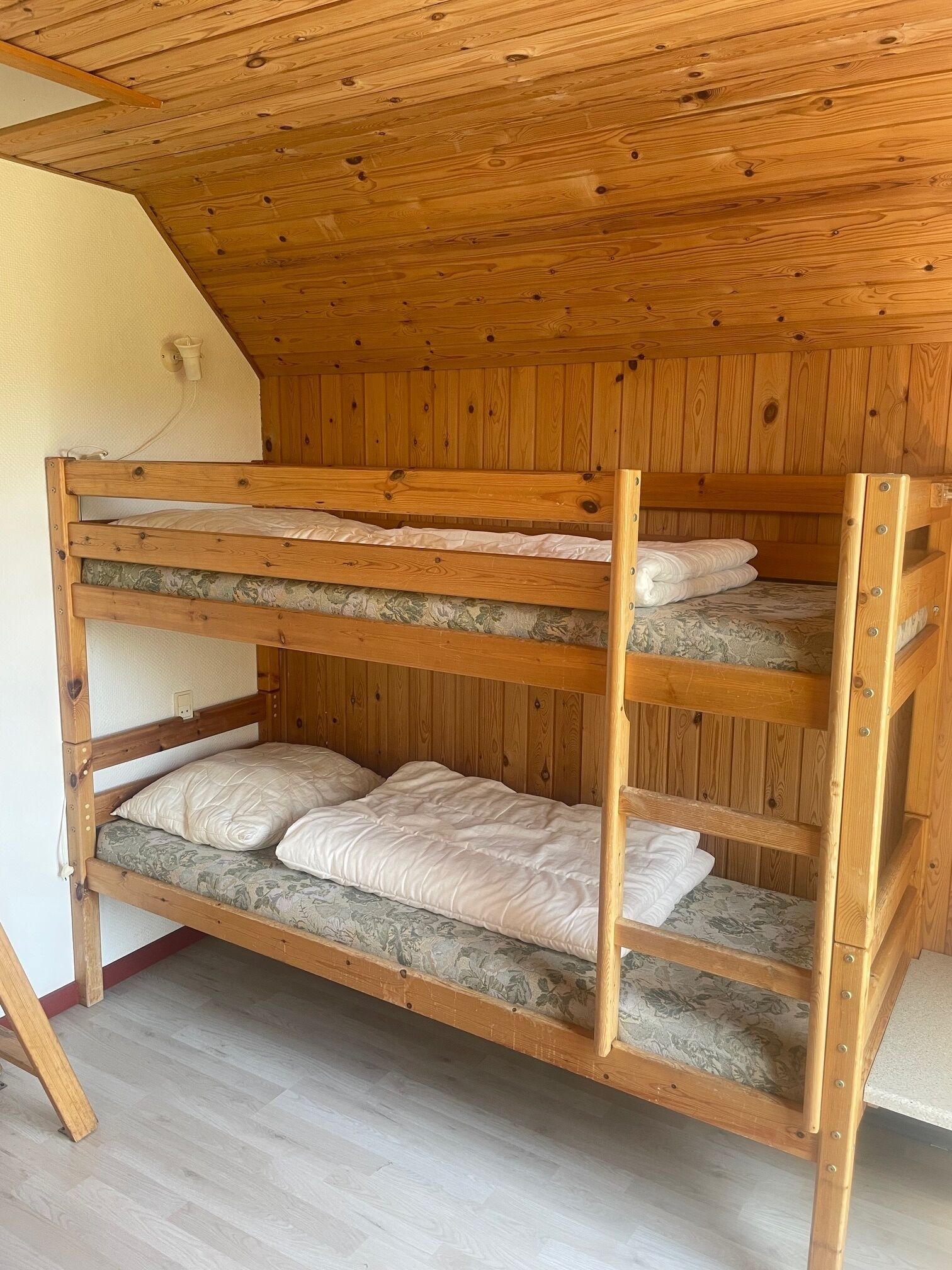 Uma cama beliche com três níveis, paredes de madeira e teto inclinado.