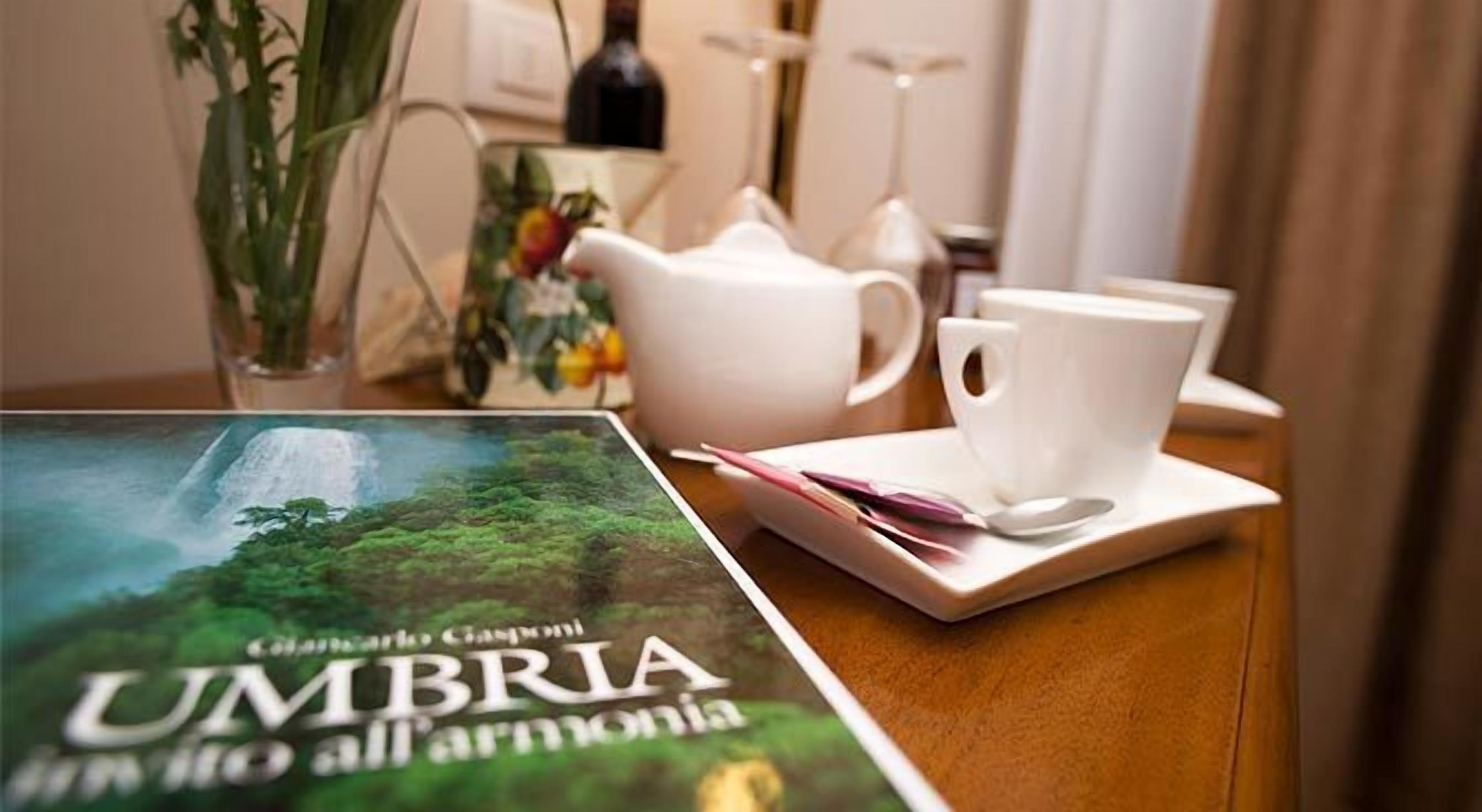 Uma mesa com um livro intitulado 'Umbria', uma chaleira branca e uma xícara branca sobre uma bandeja.