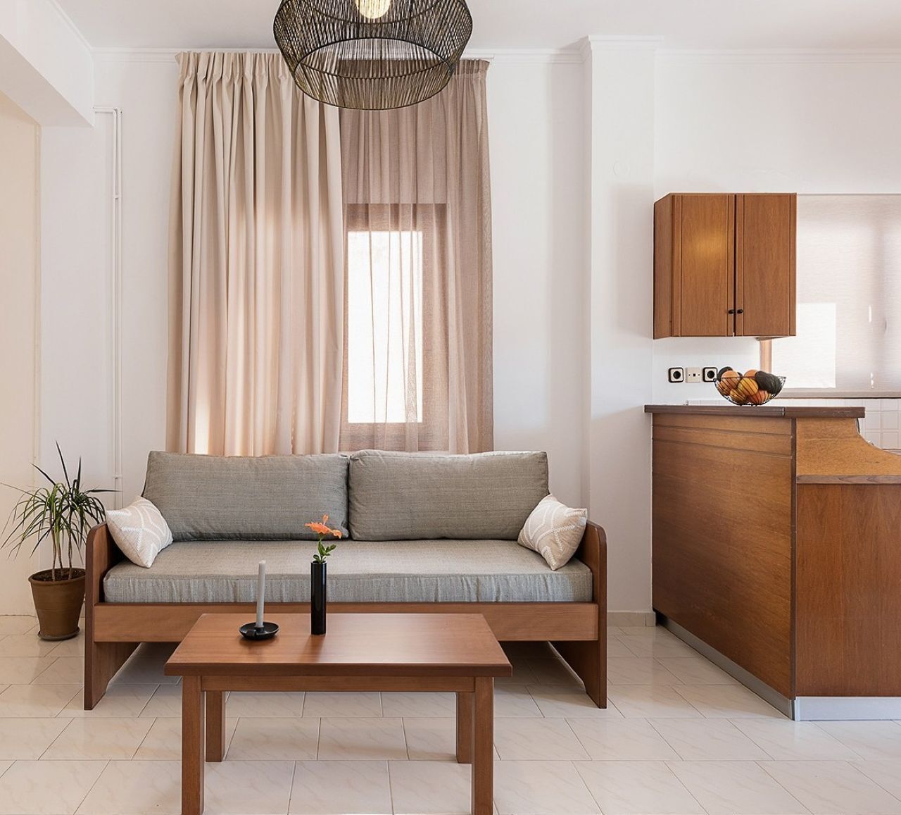 Uma sala de estar moderna com um sofá, uma mesa de centro, uma planta em vaso e uma área de cozinha com armários de madeira.