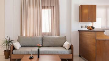 Uma sala de estar moderna com um sofá, uma mesa de centro, uma planta em vaso e uma área de cozinha com armários de madeira.