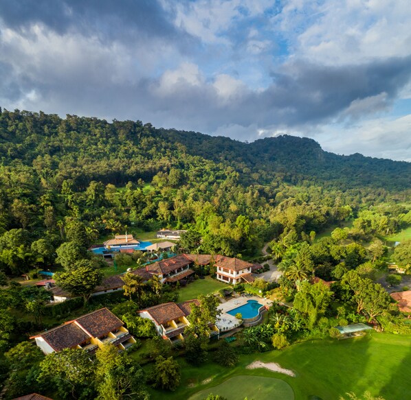 Vista aérea de um resort com vários edifícios, piscina e vegetação exuberante.