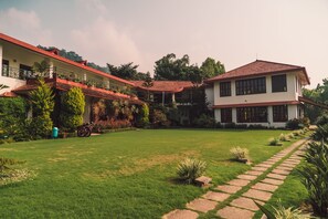 Um edifício grande de dois andares, com telhado vermelho e paredes brancas, rodeado por um jardim e relvado bem cuidados.