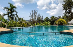 Piscina azul límpida rodeada por vegetação tropical e um céu claro.