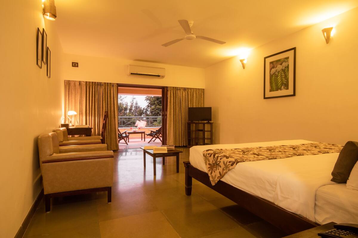 Quarto de hotel com cama, televisão, ventoinha no teto, escrivaninha e cadeira.