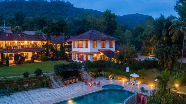 Uma casa de dois andares com piscina, cercada por vegetação exuberante e uma paisagem montanhosa.