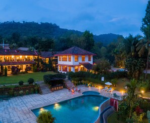 Uma casa de dois andares com piscina, cercada por vegetação exuberante e uma paisagem montanhosa.