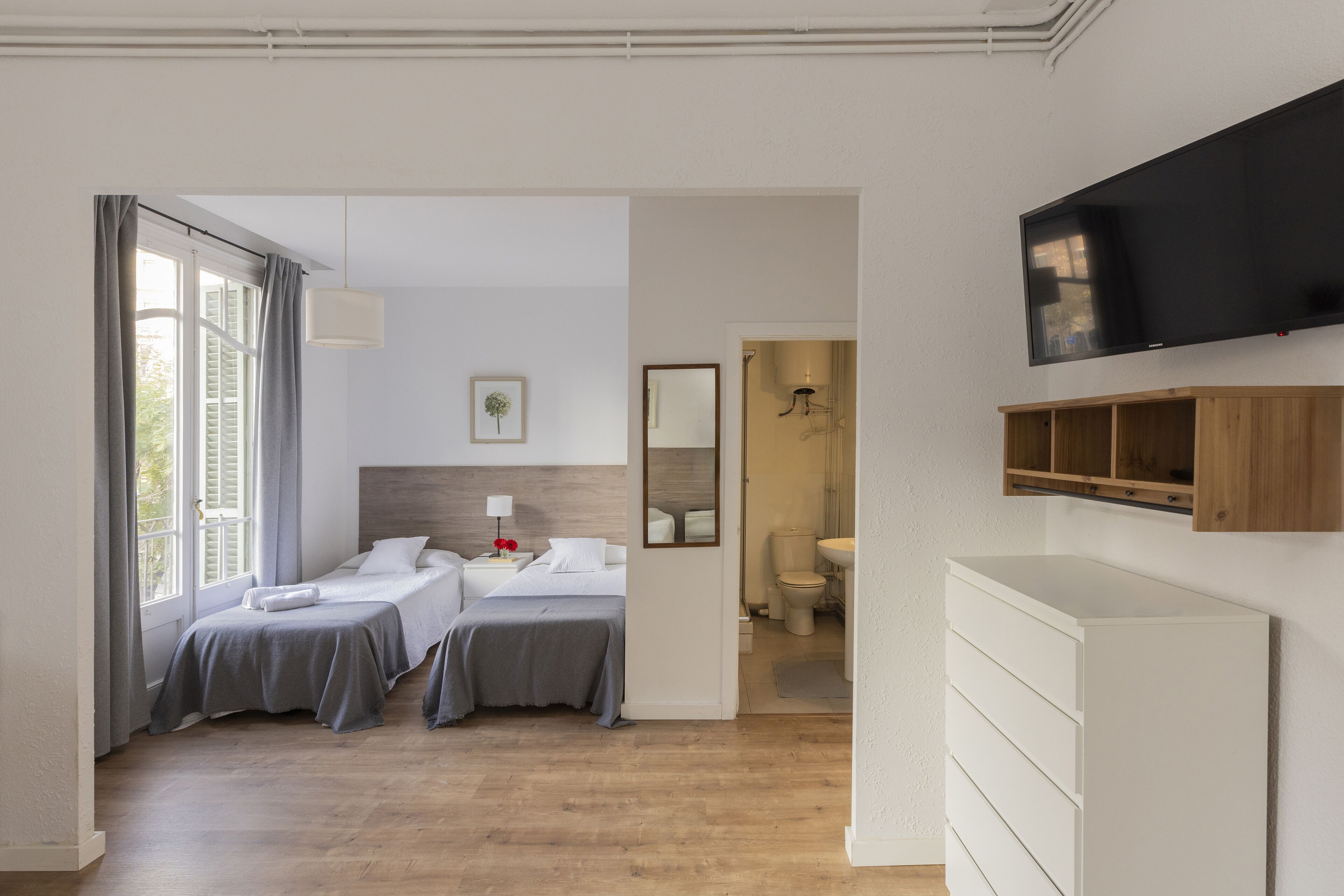 Quarto de hotel com duas camas, televisão, cómoda de madeira e banheiro visível através de uma porta aberta.