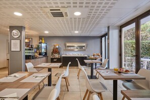 Um restaurante moderno com mesas, cadeiras, um balcão e vista para o verde lá fora.