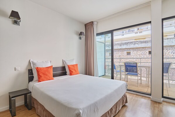 Quarto de hotel moderno com uma cama grande, uma mesinha, varanda com área de estar externa e vista para a cidade.